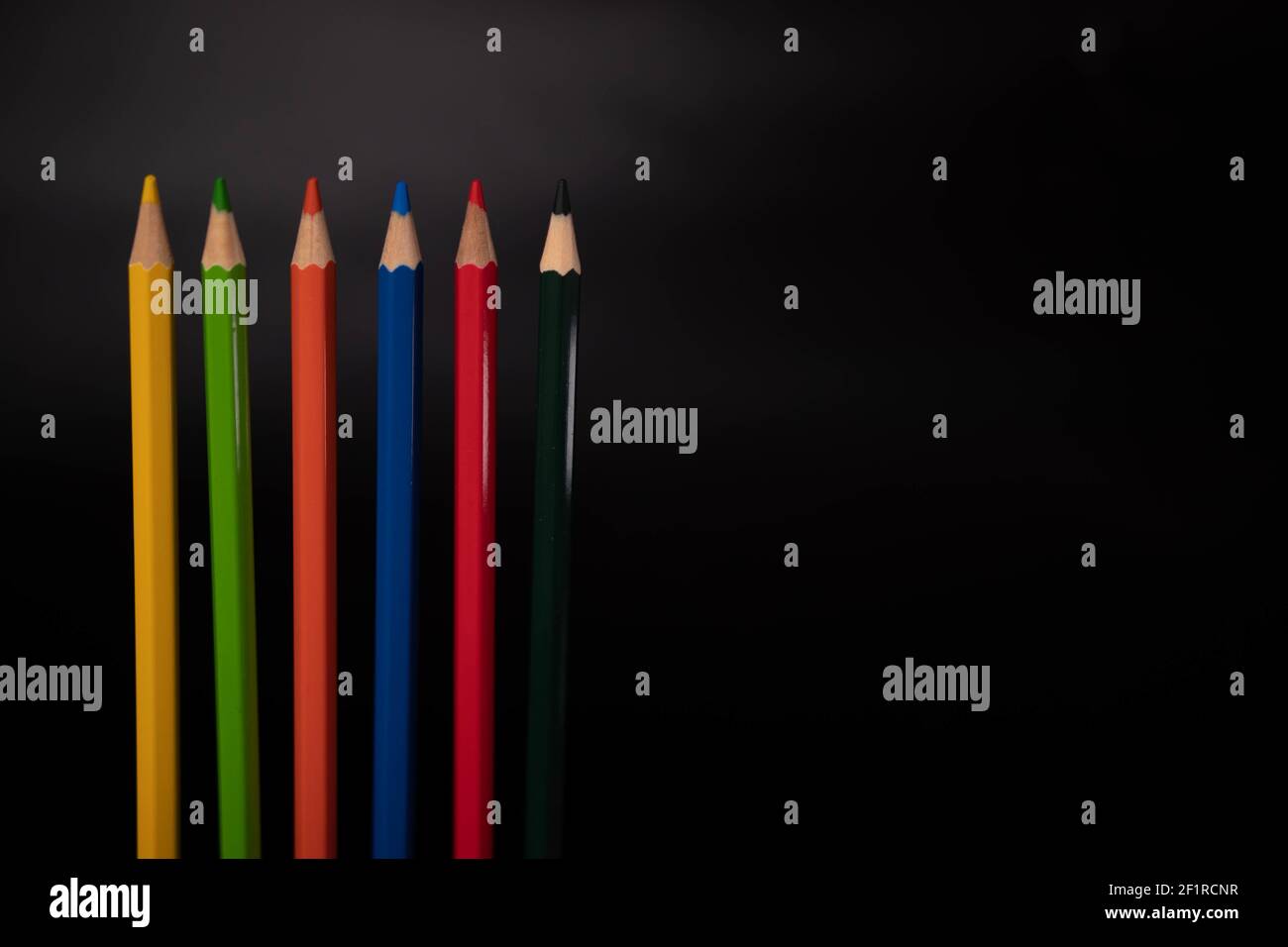 A closeup of various colored pencils put together in a line on a black ...