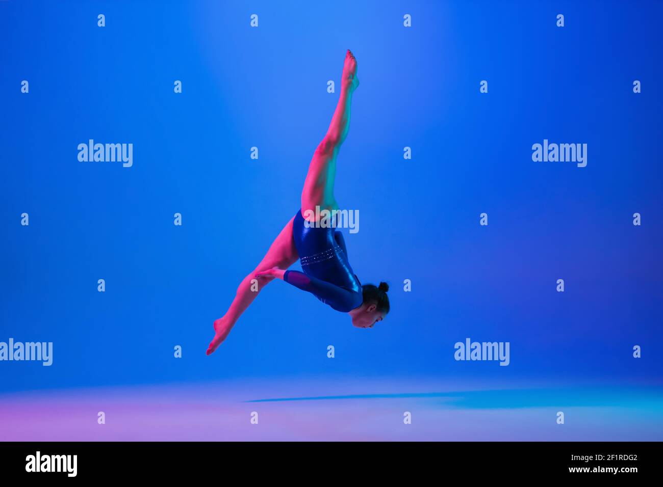 Flying high. Young flexible girl isolated on blue studio background in ...