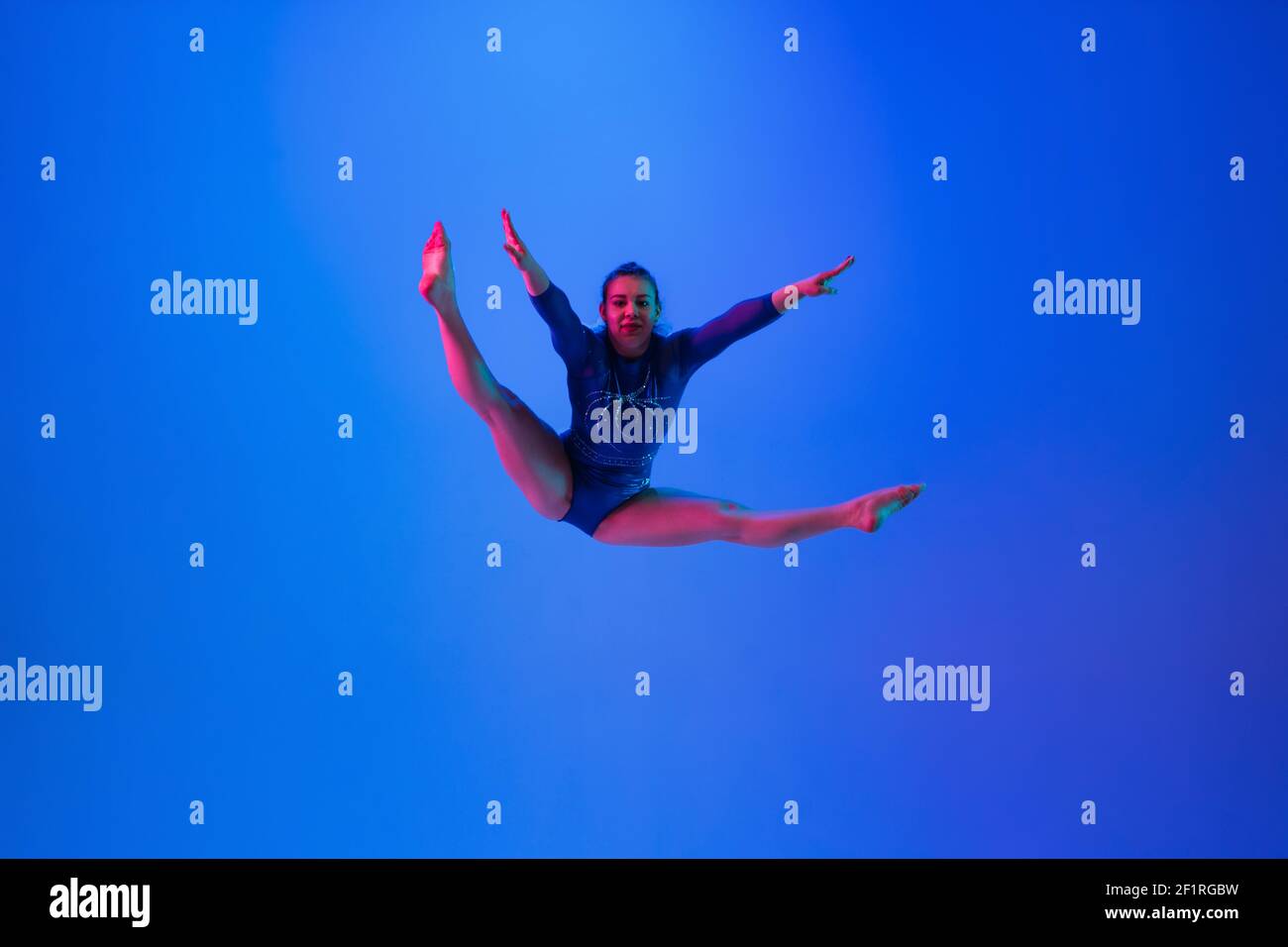 Flying high. Young flexible girl isolated on blue studio background in ...