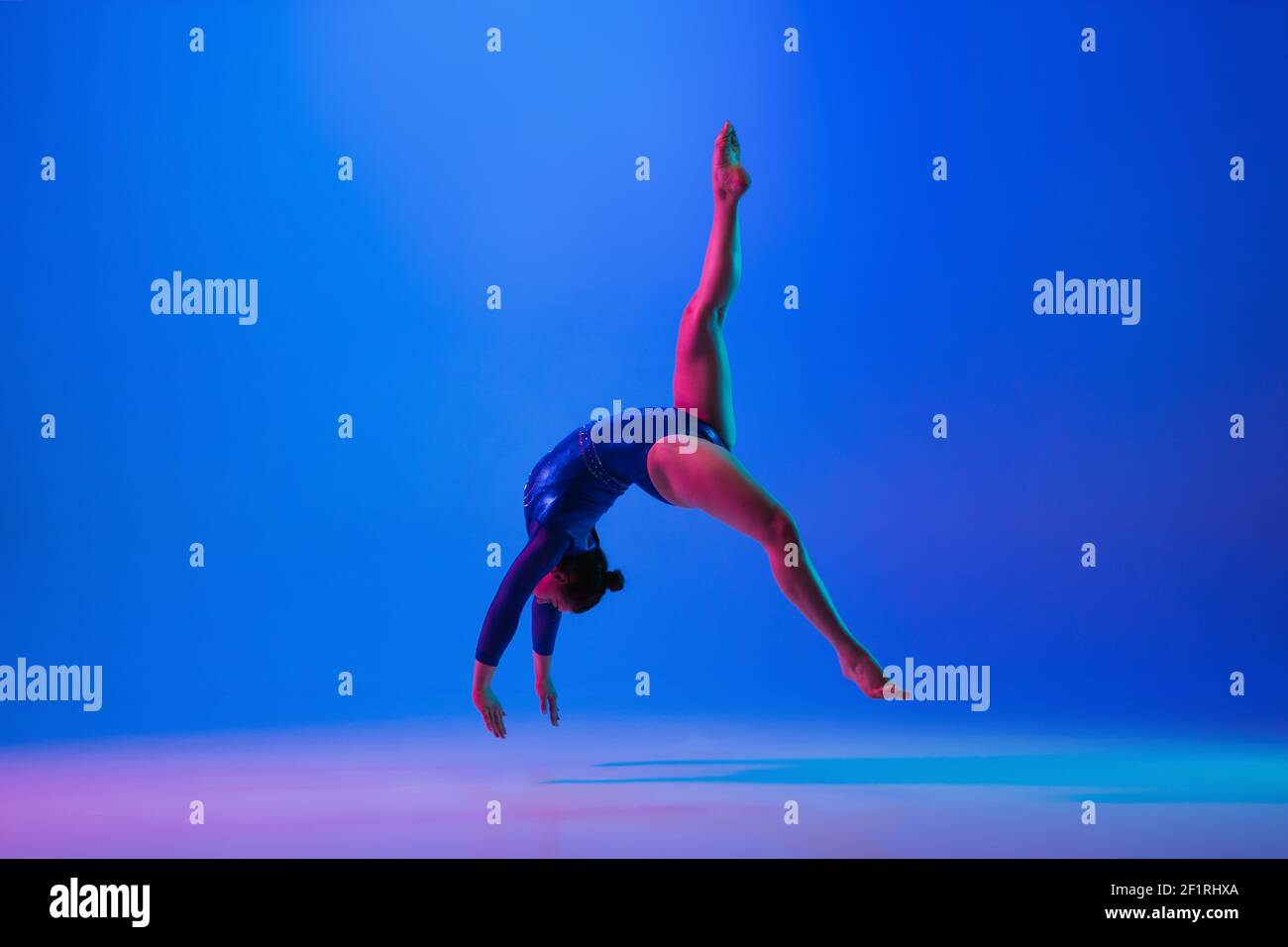 Flying high. Young flexible girl isolated on blue studio background in ...