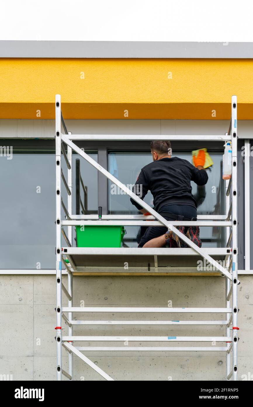 View of a man cleaning windows of a house while high up on scaffolding ...