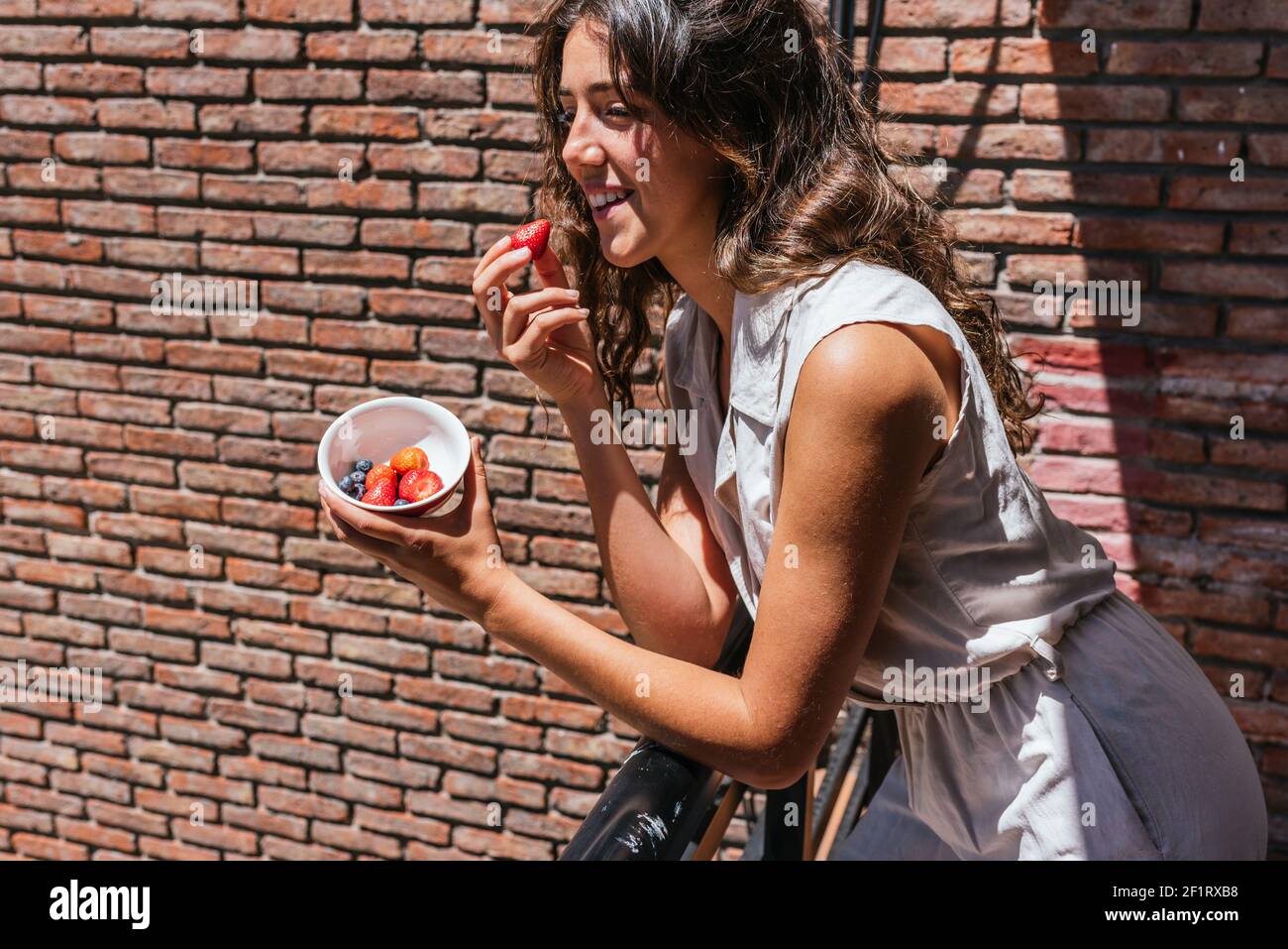 Stock photo of happy woman eating fruit in the balcony with the sun in ...