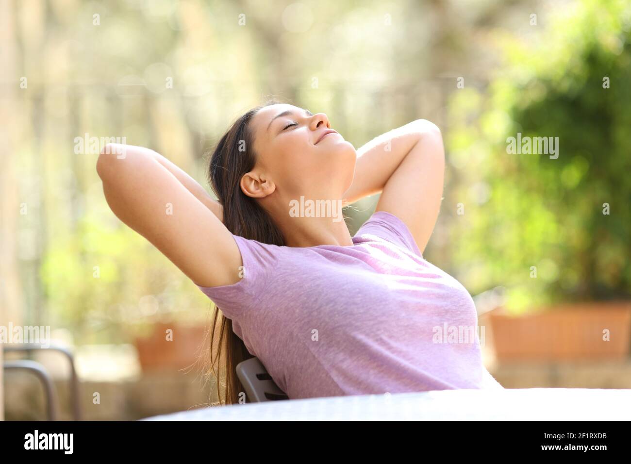 Relaxed woman resting breathing fresh air with arms on head sitting in ...