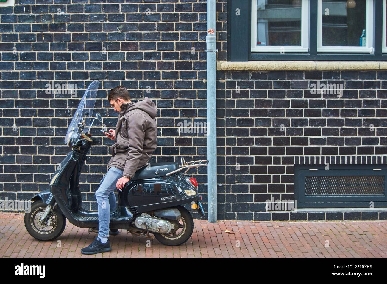 Man sitting on a stationary moped by a wall, resting and smoking Stock ...