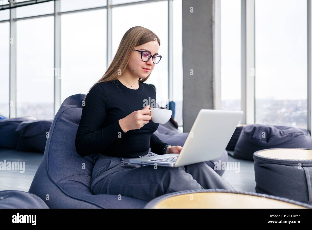 A successful young woman manager sits with a laptop on a soft armchair ...