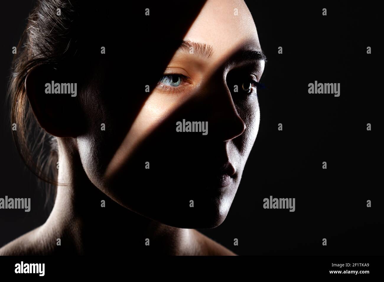 studio portrait of a beautiful young woman with shadows on her face ...