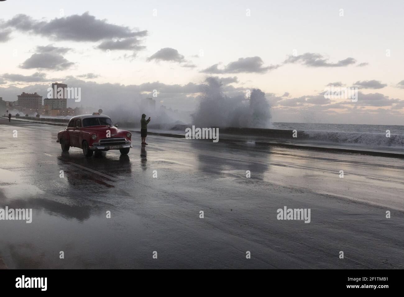 Cuba, Havana - Old car driving past waves splashing up on the Malecon ...