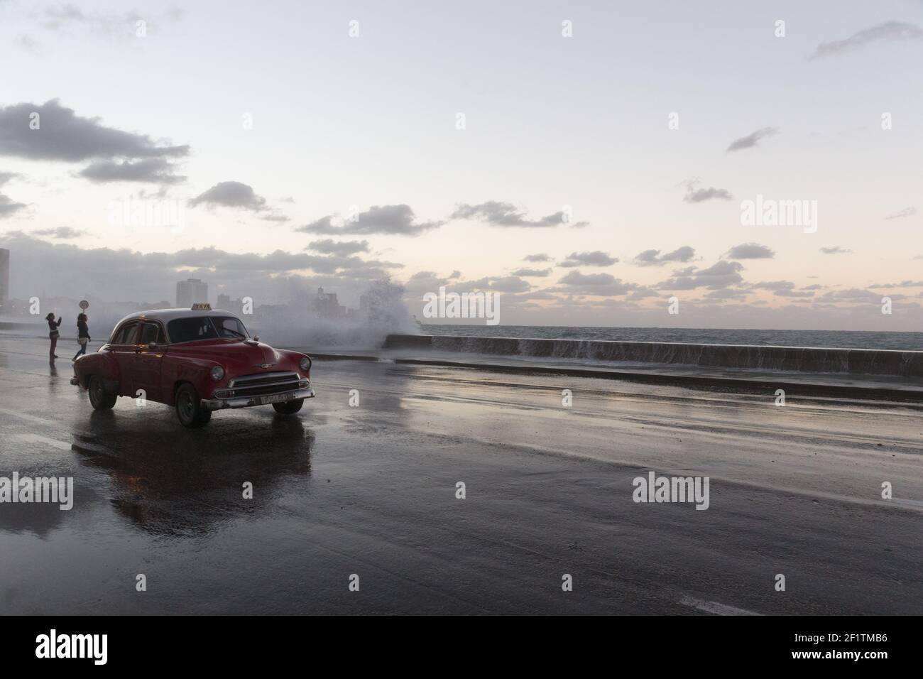 Cuba, Havana - Old car driving past waves splashing up on the Malecon ...