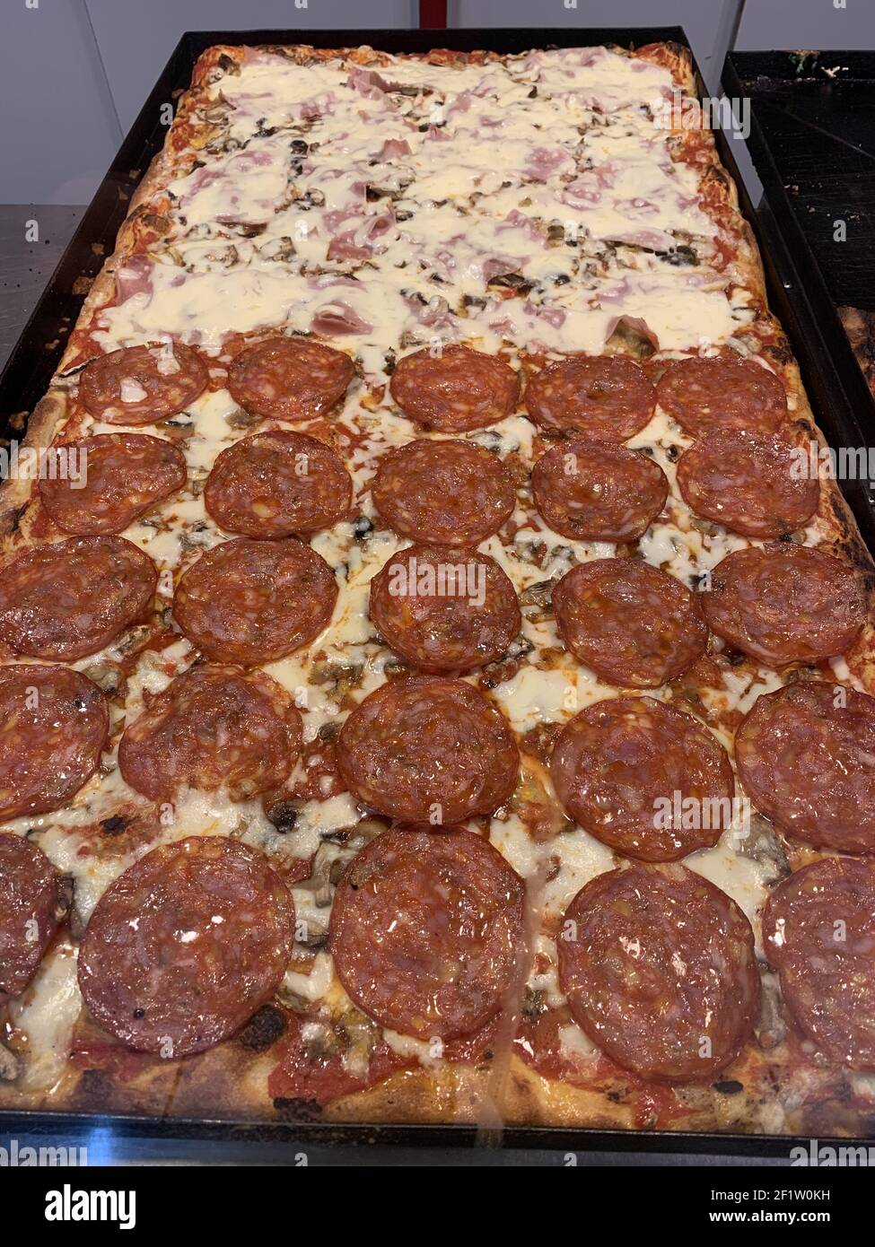 A vertical shot of a huge baked pizza with sausages, ketchup, and ...