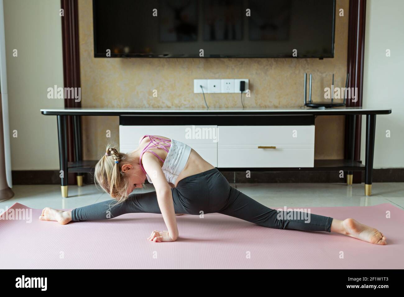 Cute little girl in sportswear doing fitness exercises at home. Distant ...