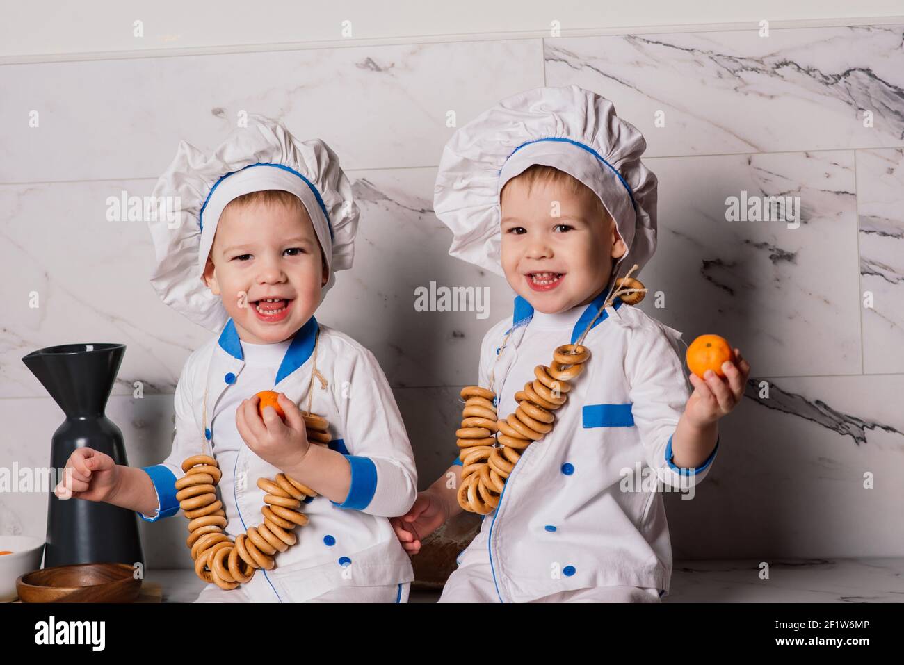 Little cute cook with cutlery sitting on kitchen, twin brothers ...