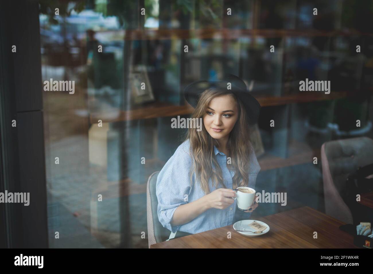 A shallow focus of a young Caucasian female with a fedora hat drinking ...