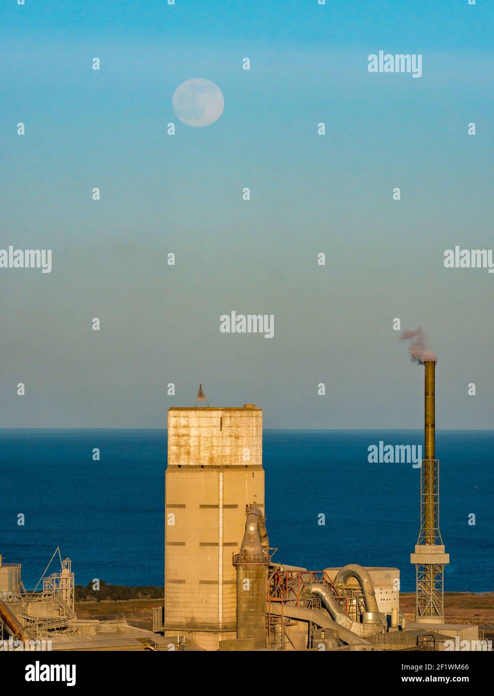 Full snow moon rising over industrial tower at sunset, Dunbar cement ...