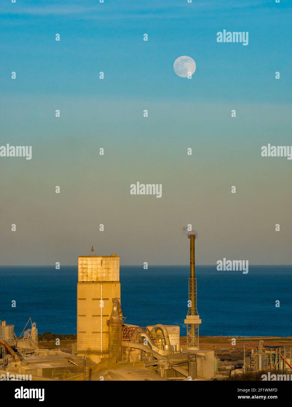 Full snow moon rising over industrial tower at sunset, Dunbar cement ...
