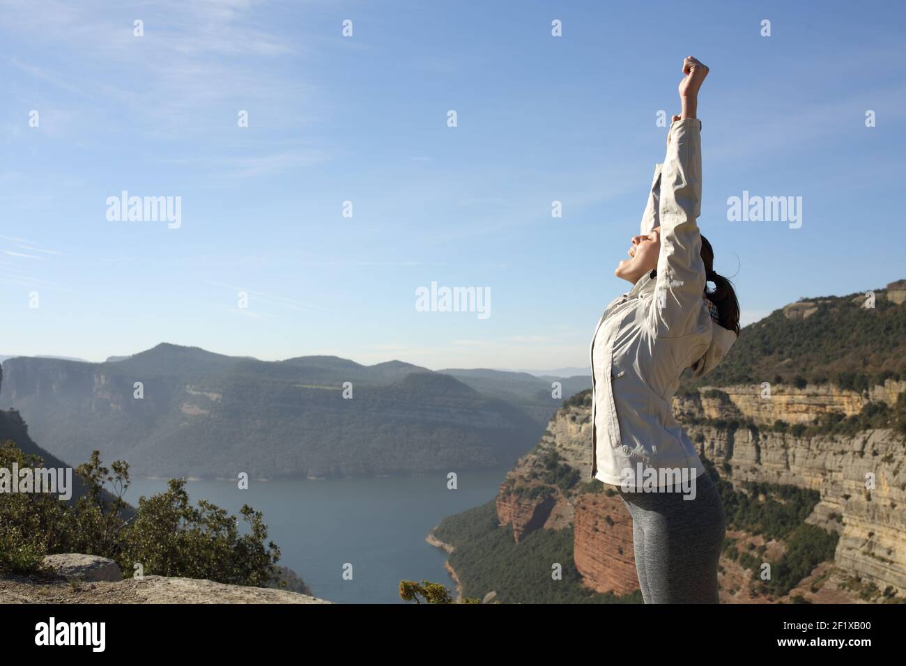 Happy trekker raising arms celebrating success in the top of a cliff in ...
