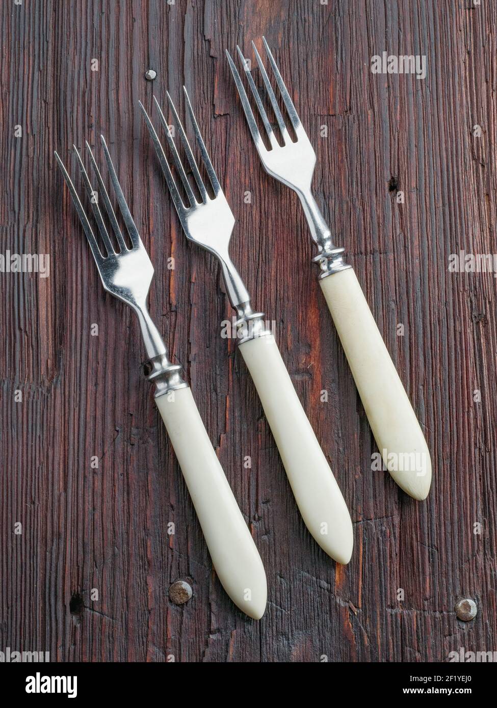 Three vintage forks. Old wooden table with nail caps and holes. Close ...