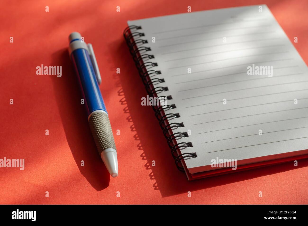 Opened notepad and blue pen on a red background with shadows. Spring ...