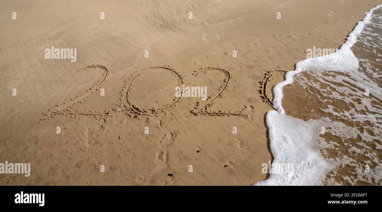 The year 2020 in tet written in sand on beach is covered by ocean wave ...