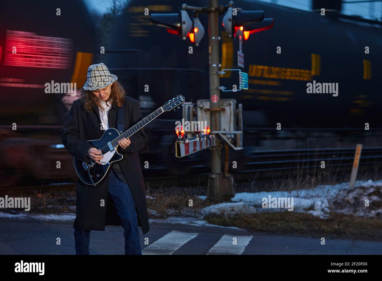Man in hat and coat playing electric guitar near train and railway ...