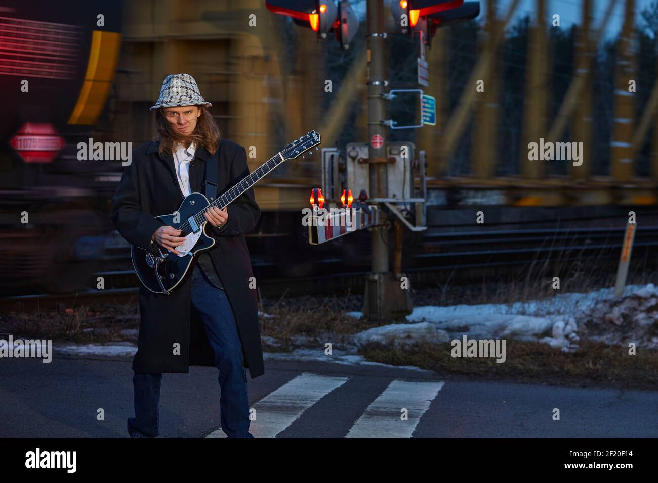 Man in hat and coat playing electric guitar near train and railway ...
