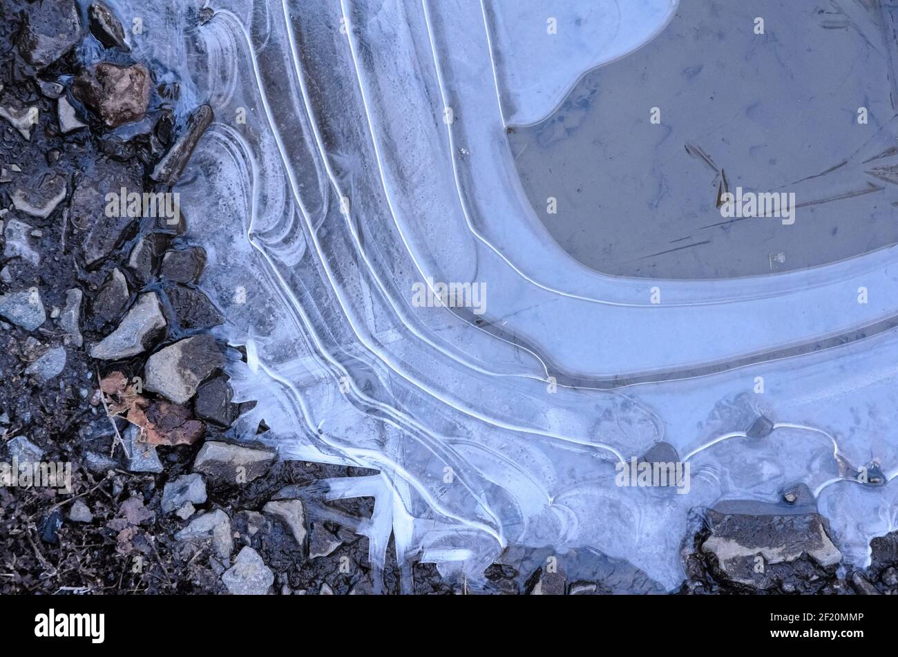 Frozen water in a puddle on the ground with abstract structures and ...