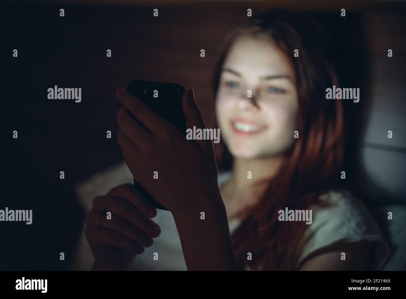 pretty woman lying in bed with phone in hand at night rest before ...