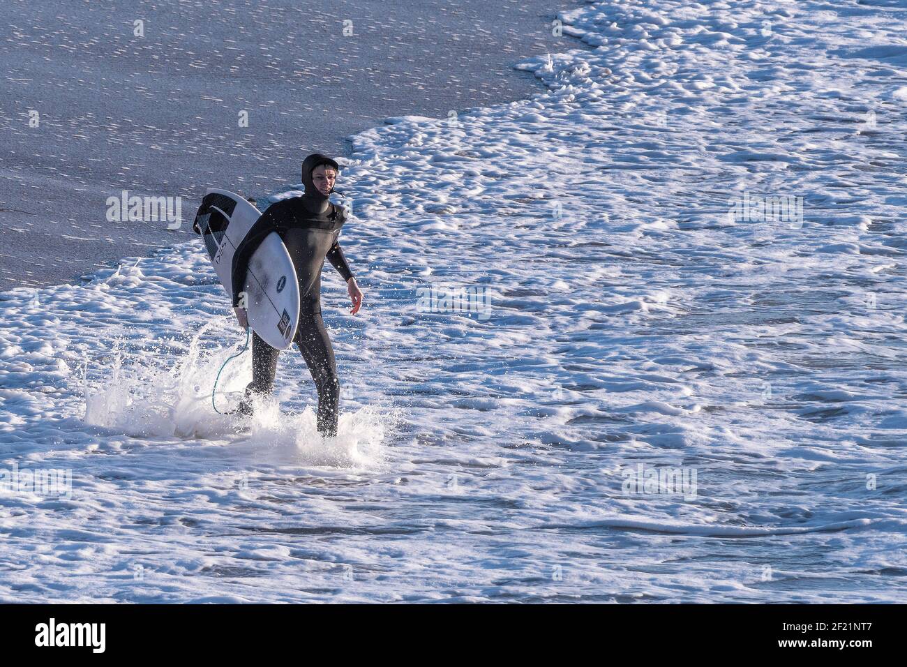 A surfer carrying his surfboard running into the sea at Fistral in ...