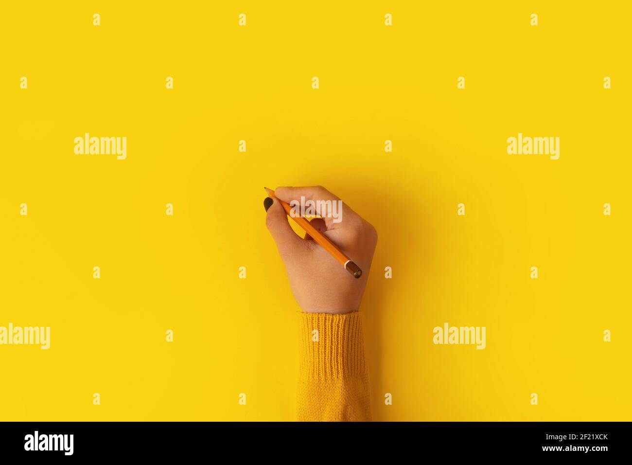 Woman's hand holding a pencil over yellow background Stock Photo - Alamy