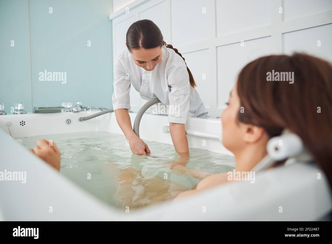 Female spa professional putting hands with hydromassage hose below ...