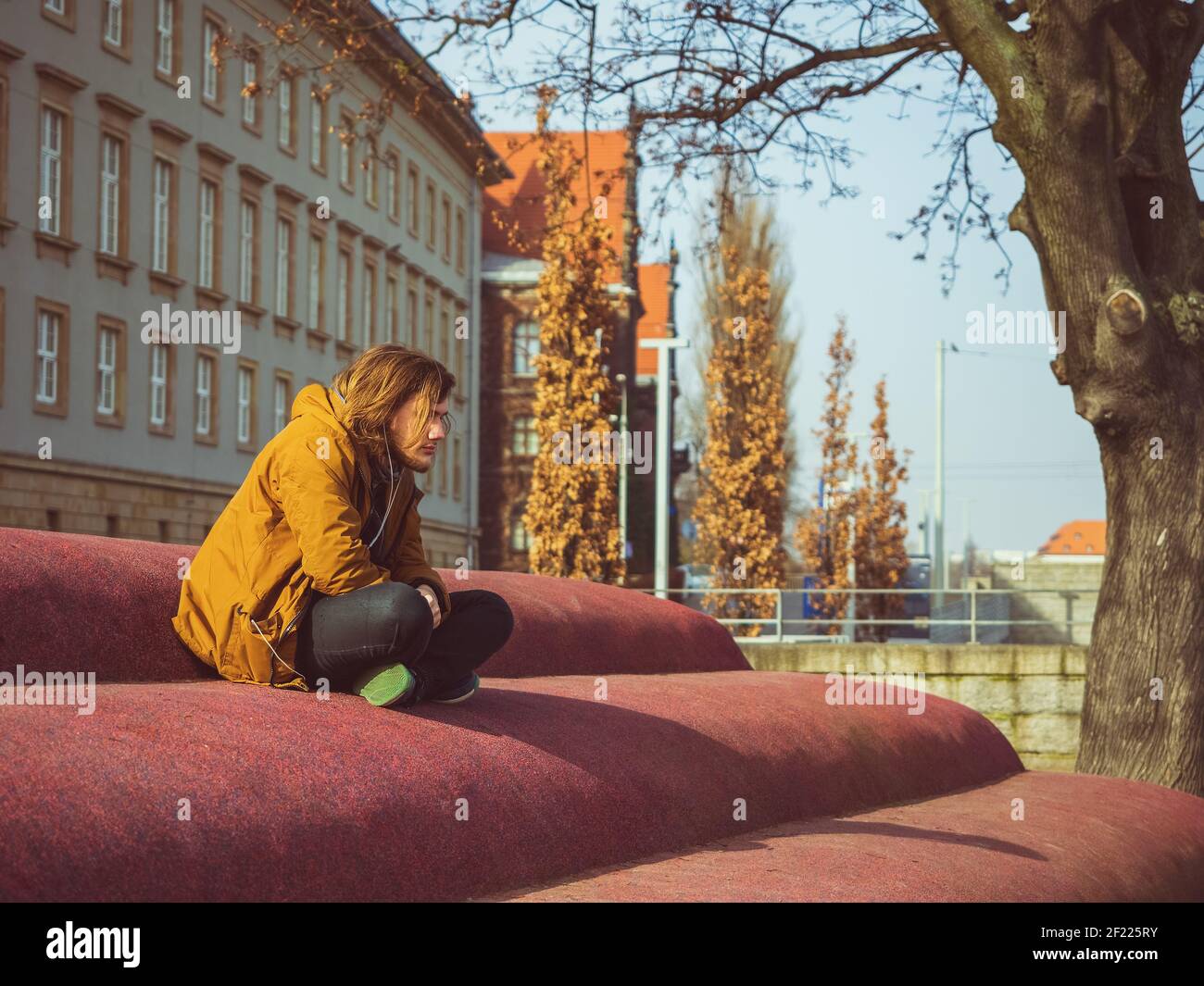 Sad young man sitting alone in a city, on urban space and watching on a ...