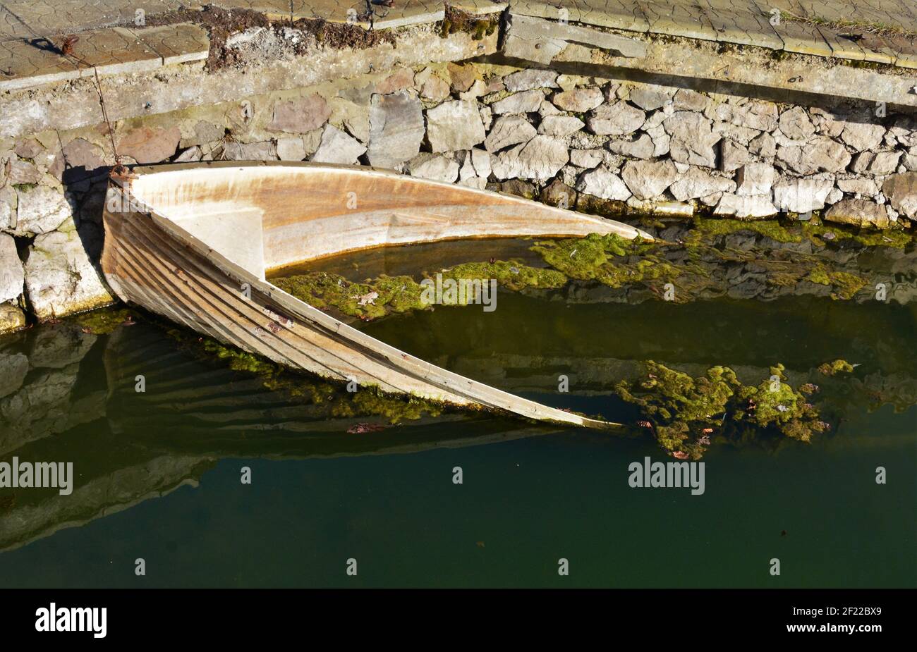 A half sunken dirty and weathered boat covered in moss in the lake ...