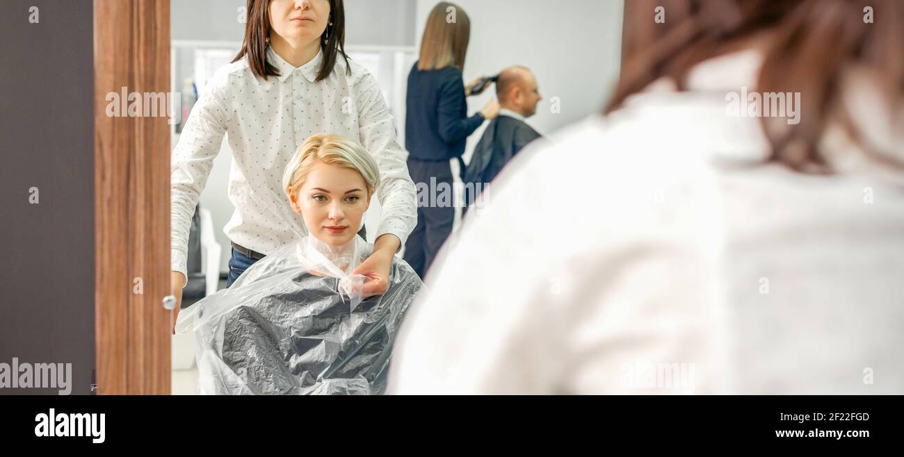 The female hairdresser puts on a transparent cellophane cape to the ...