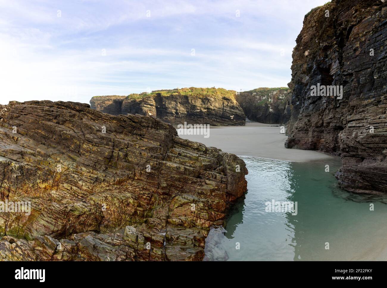 A sandy beach with tidal pools and jagged broken cliffs behind in warm ...