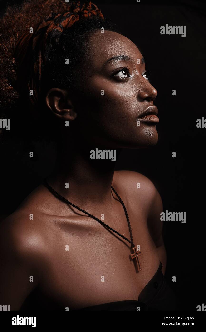 Side view of beautiful african christian woman stands on black ...