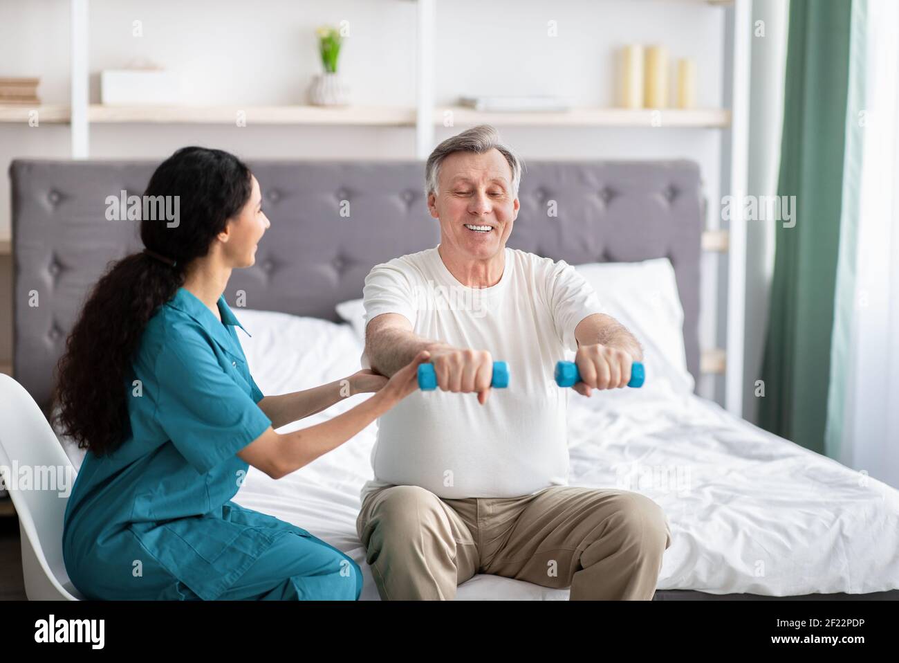 Young physiotherapist helping homebound elderly man to do physical ...