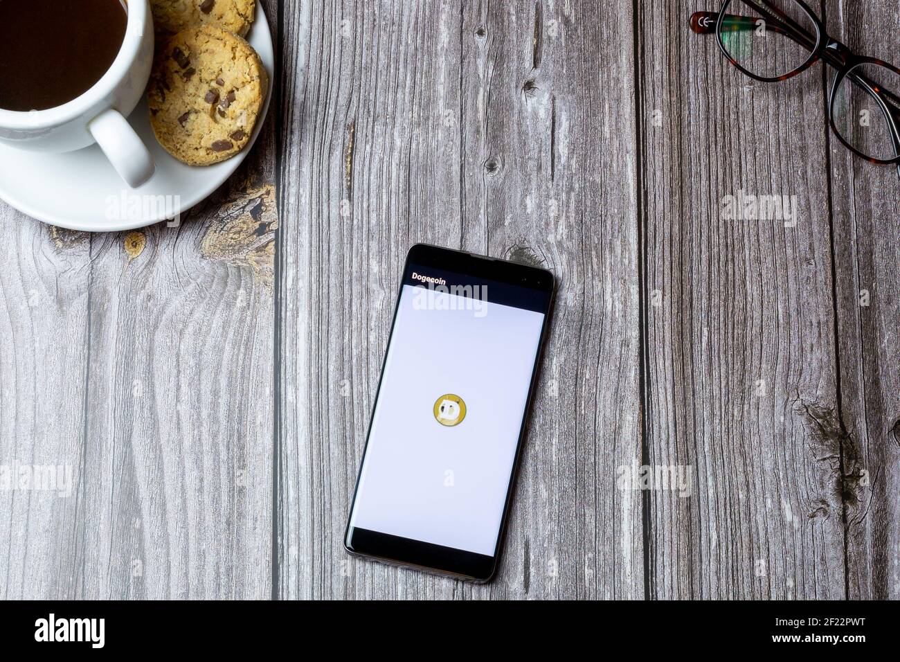 A mobile phone or cell phone laid on a wooden table with the Dogecoin ...