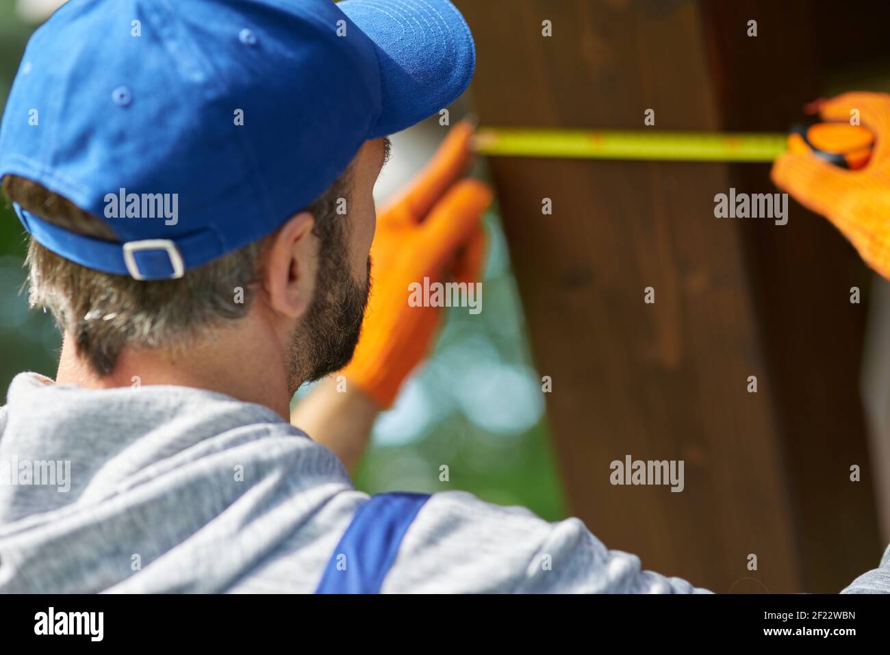 Close up of young workman wearing blue cap and overalls using measuring ...