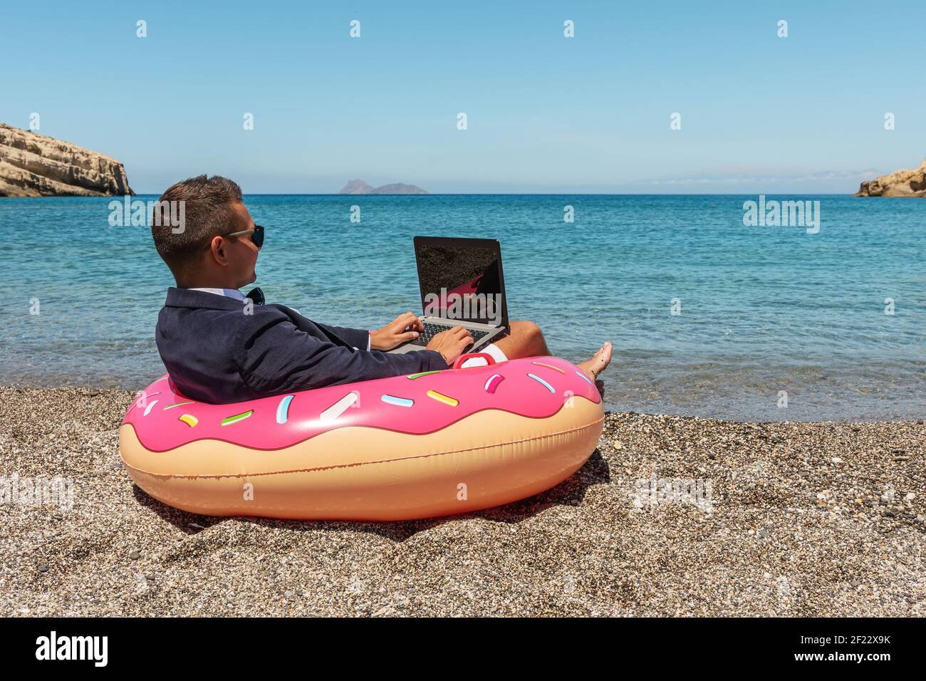 Businessman using laptop computer on inflatable donut on tropical beach ...
