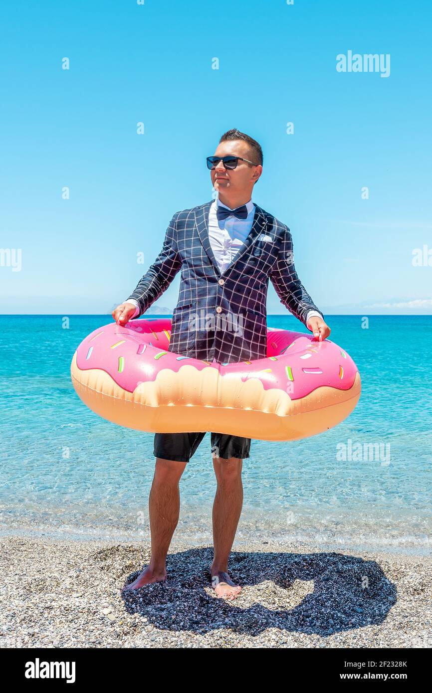 Happy businessman in a jacket with an inflatable donut on a tropical ...
