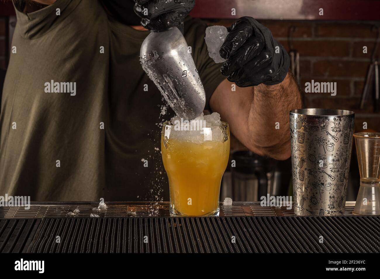 The bartender at the bar pours ice into an orange alcoholic cocktail. Summer party background ...