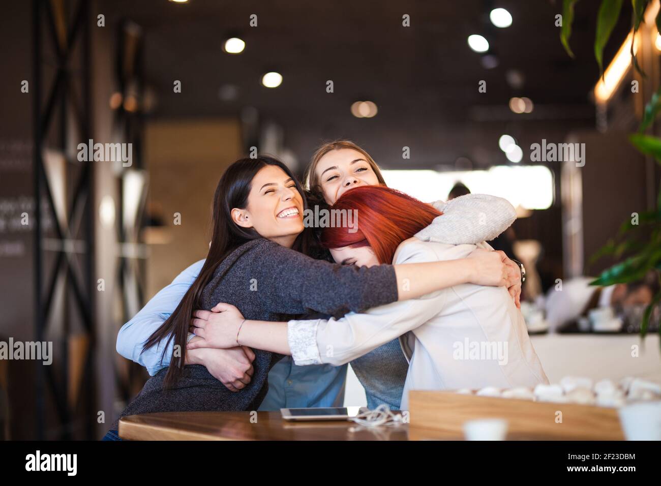 Four friends at a cafe celebrating and hugging. Successful young people ...
