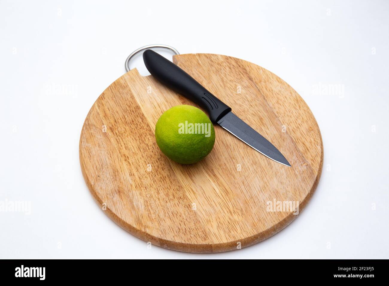 A lime and a knife on a round wooden cutting board isolated on a white ...