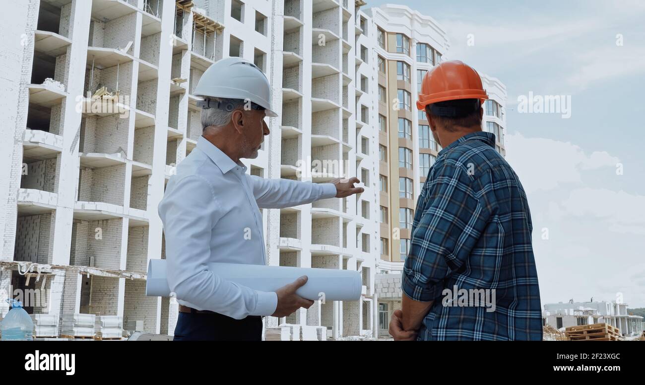 Engineer with blueprints pointing with hand while talking with builder ...