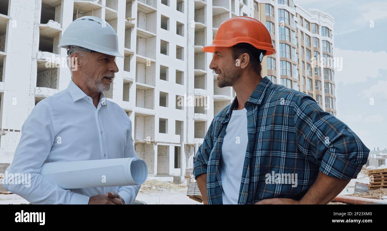 Engineer with blueprints talking with happy builder on construction ...