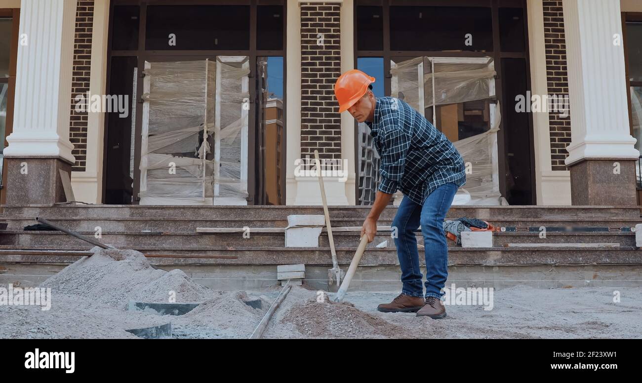 Builder digging ground with shovel near building on construction site ...
