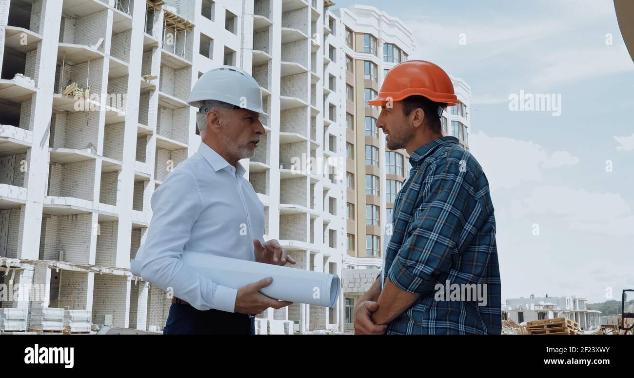 side view of engineer with blueprints talking with builder on ...