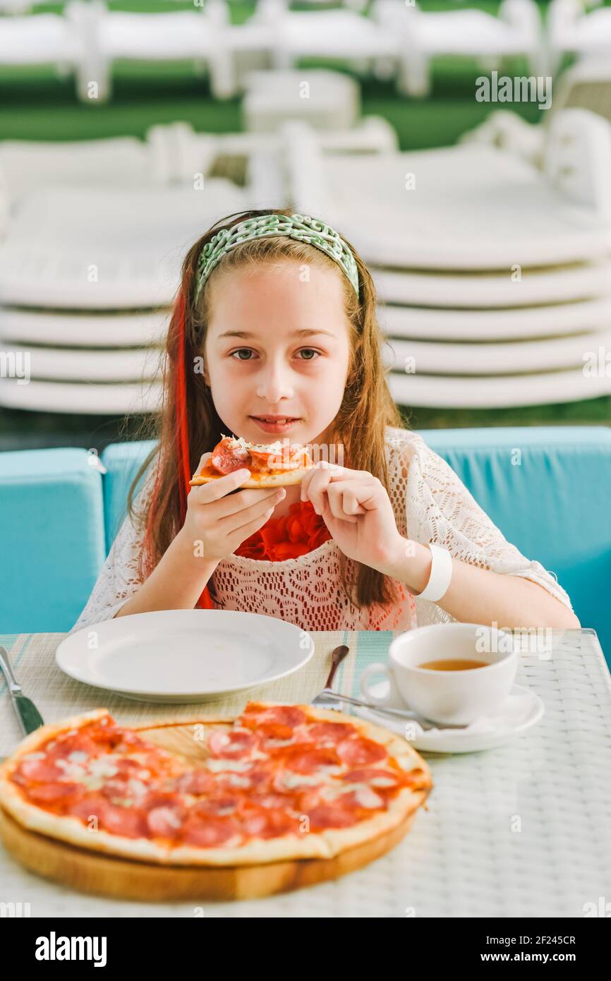 Little girl eating pizza in a summer cafe. Summer relaxation by the ...