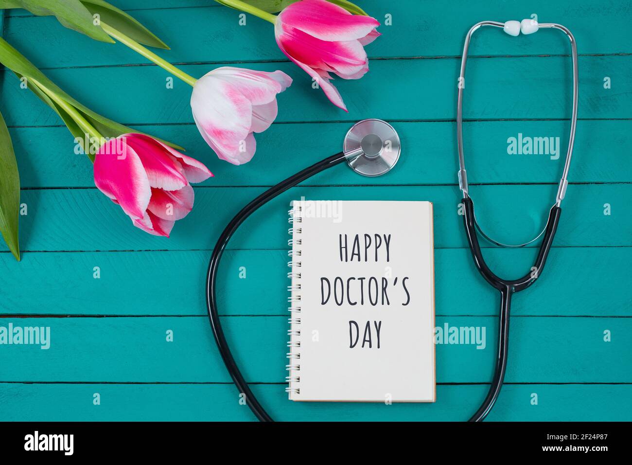Pink tulips and stethoscope with spiral notepad with Happy Doctors Day ...