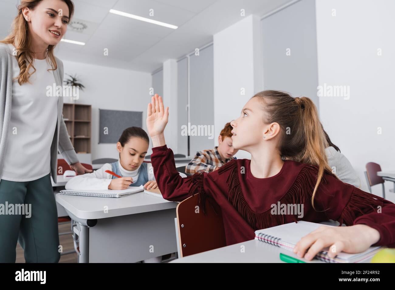 schoolgirl with raised hand looking at teacher during lesson Stock ...