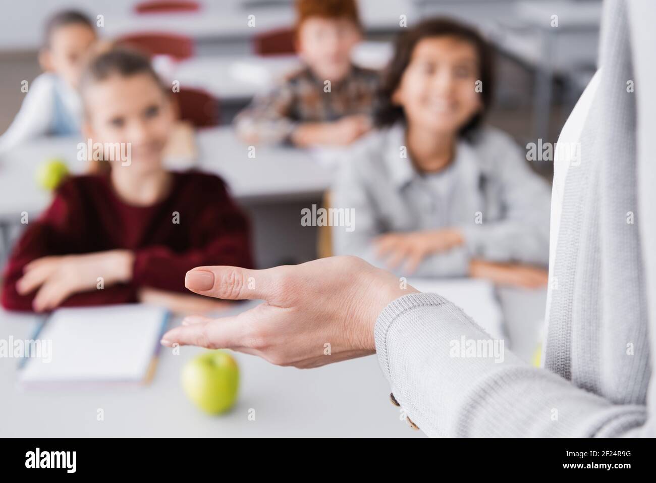 teacher gesturing during lesson near schoolkids on blurred background ...